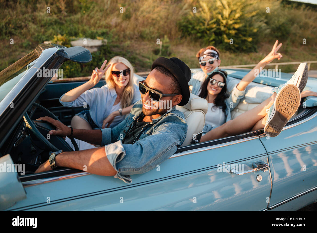 Group of smiling young friends driving car and showing peace sign in ...