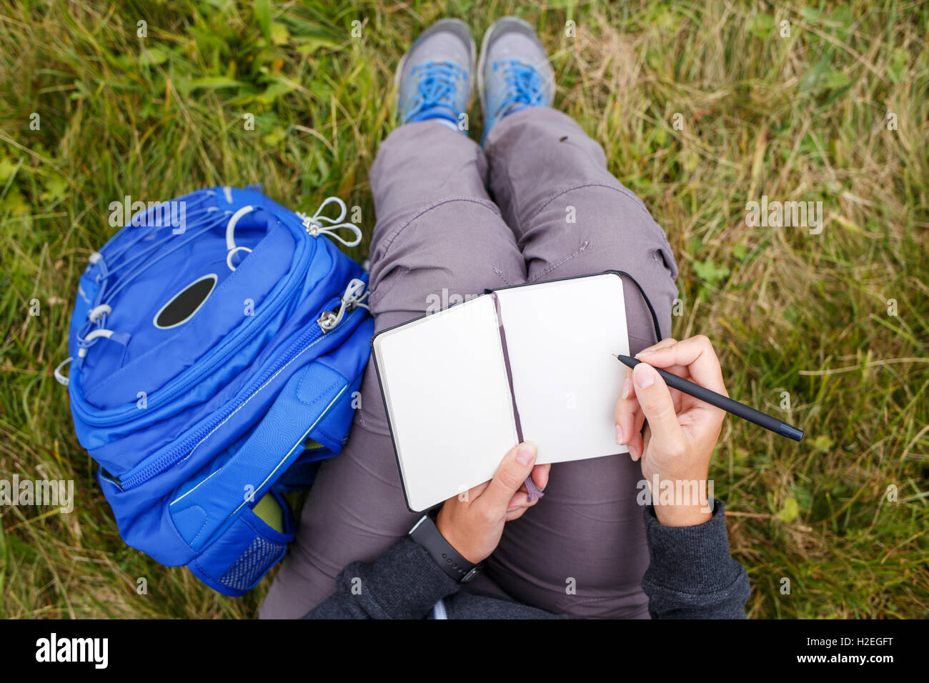 Woman with blue backpack sitting on grass and writing into blank ...