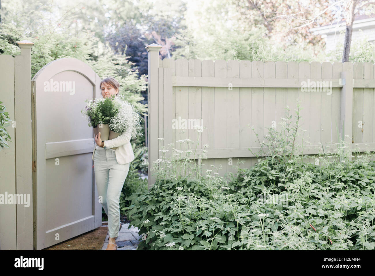 Woman entering a garden through a gate, carrying a bunch of white ...