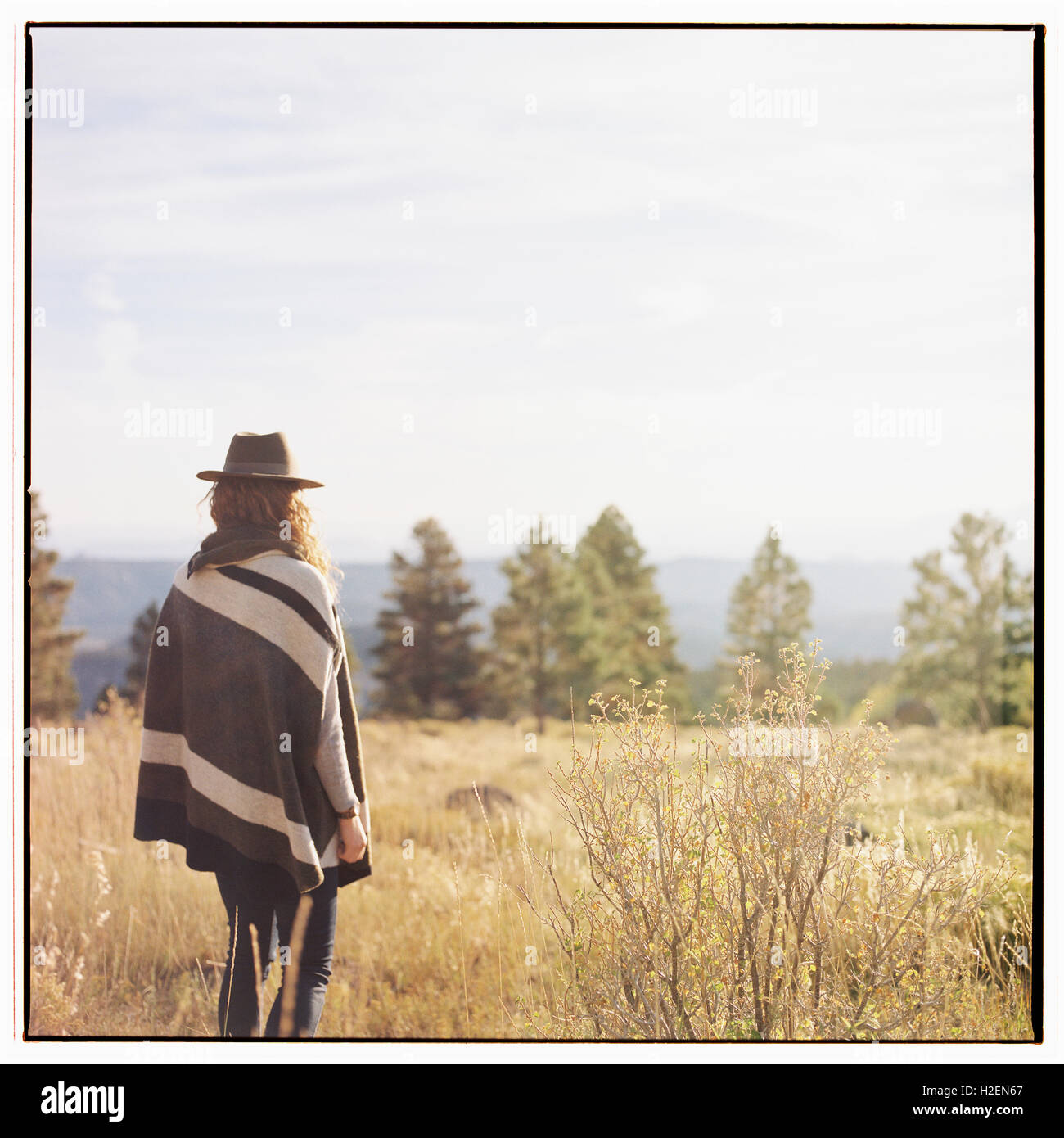 A woman with hat and pon cho standing in open space looking across ...