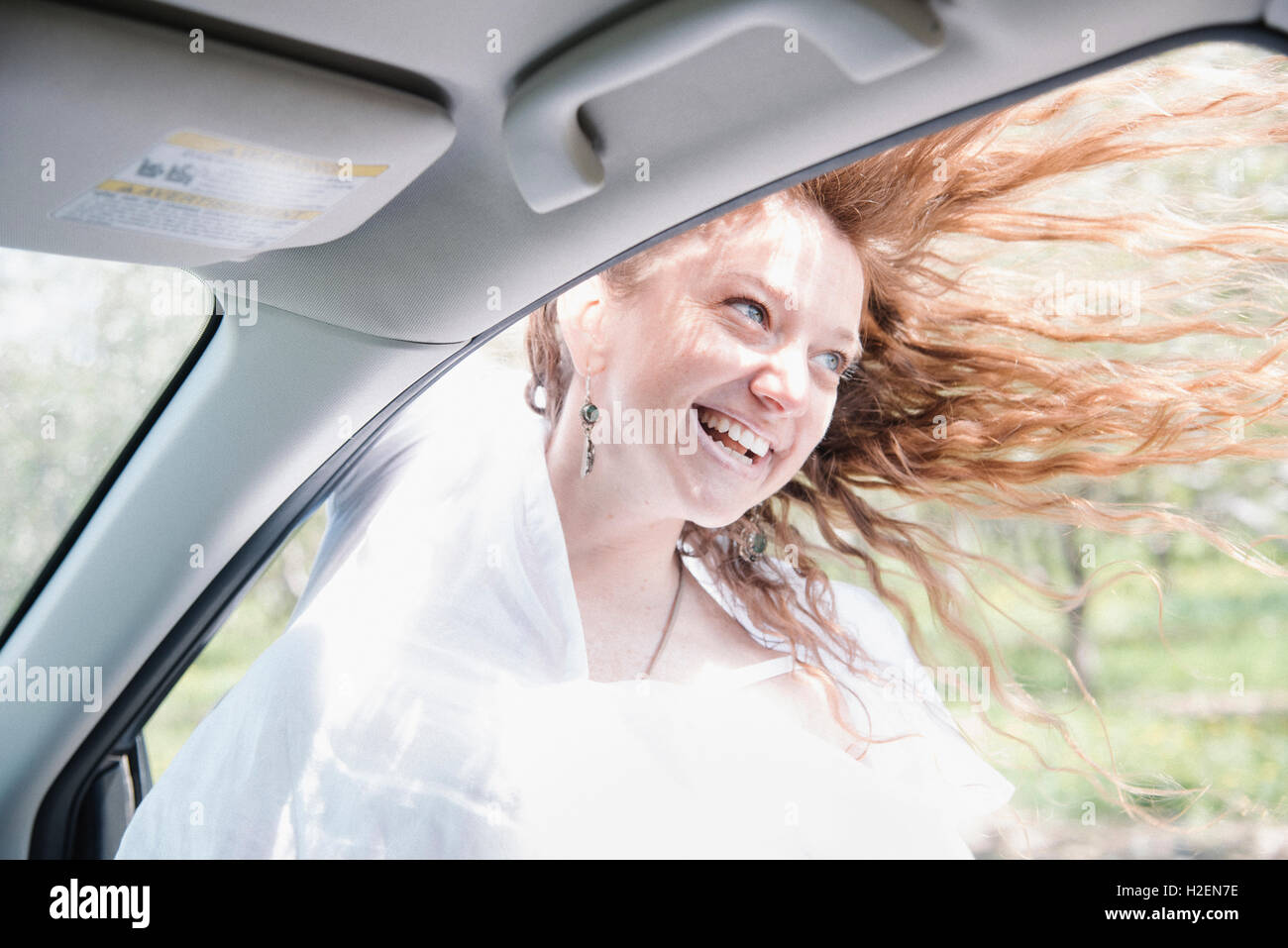 Woman on a road trip, leaning out of a car window, her lon g red hair ...