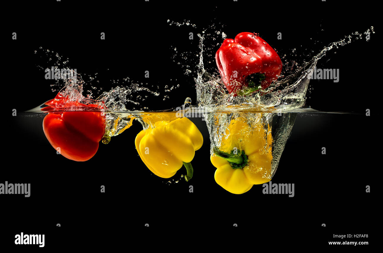Group of bell pepper falling in water with splash on black background ...