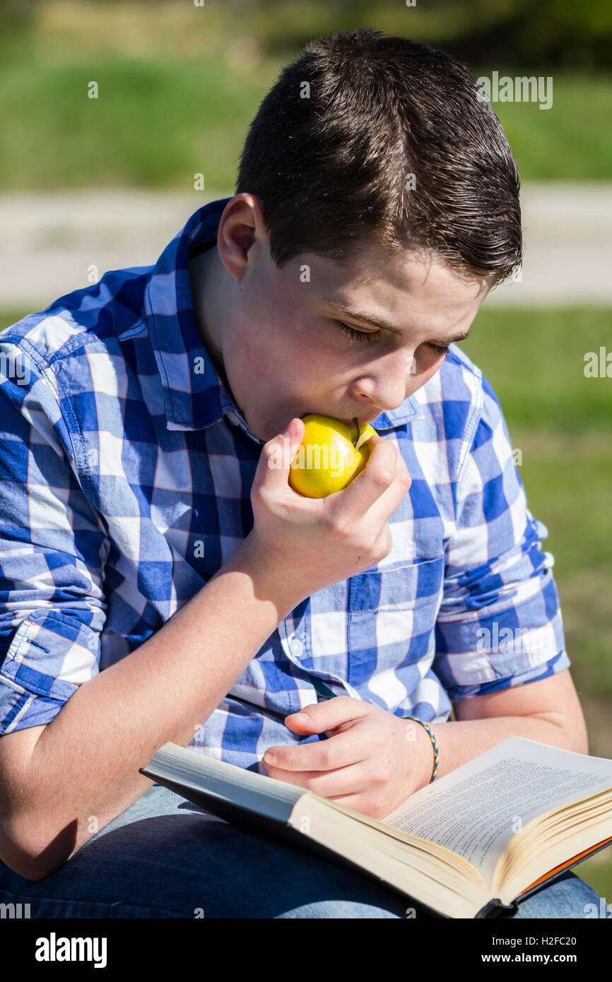 Eating.Young man reading a book in outdoor with yellow apple Stock ...