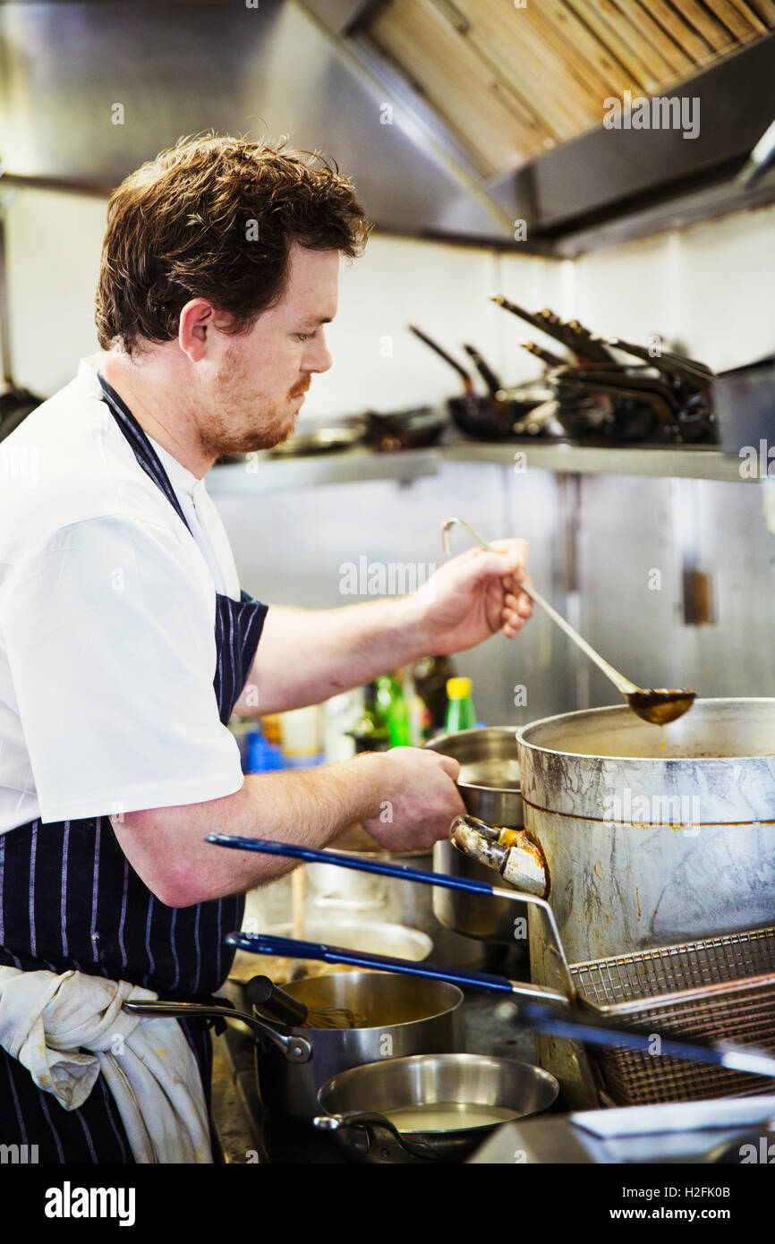 A village public house kitchen. A chef working in the kitchen, using a ...