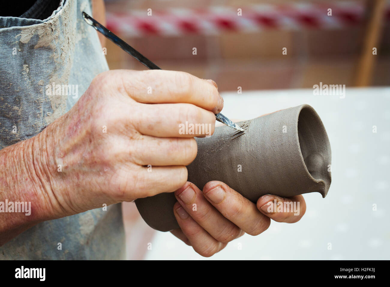 A potter handling a wet clay pot and marking a design on the outside ...