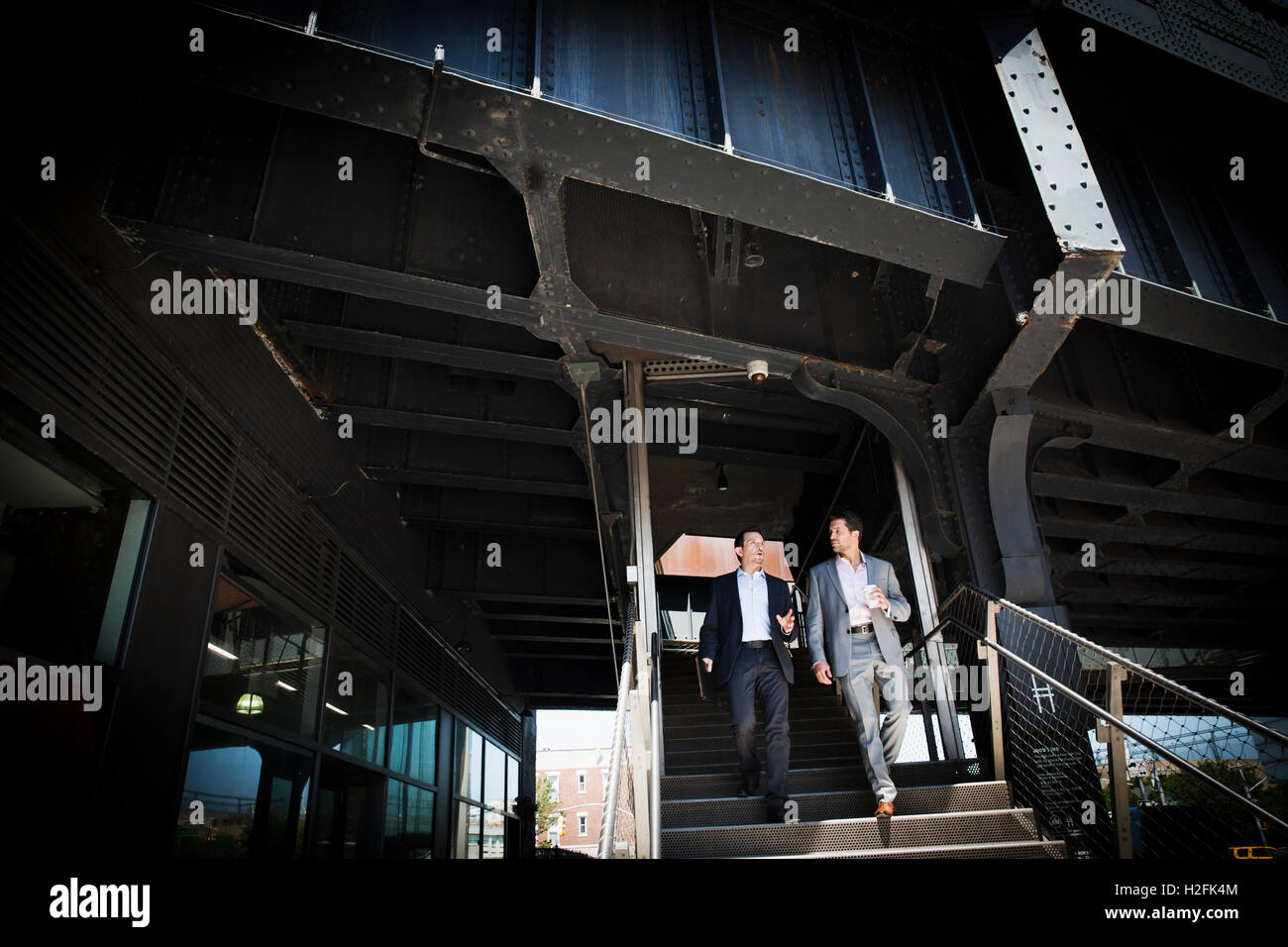 Two businessmen wearing grey suits walking down a staircase at the ...