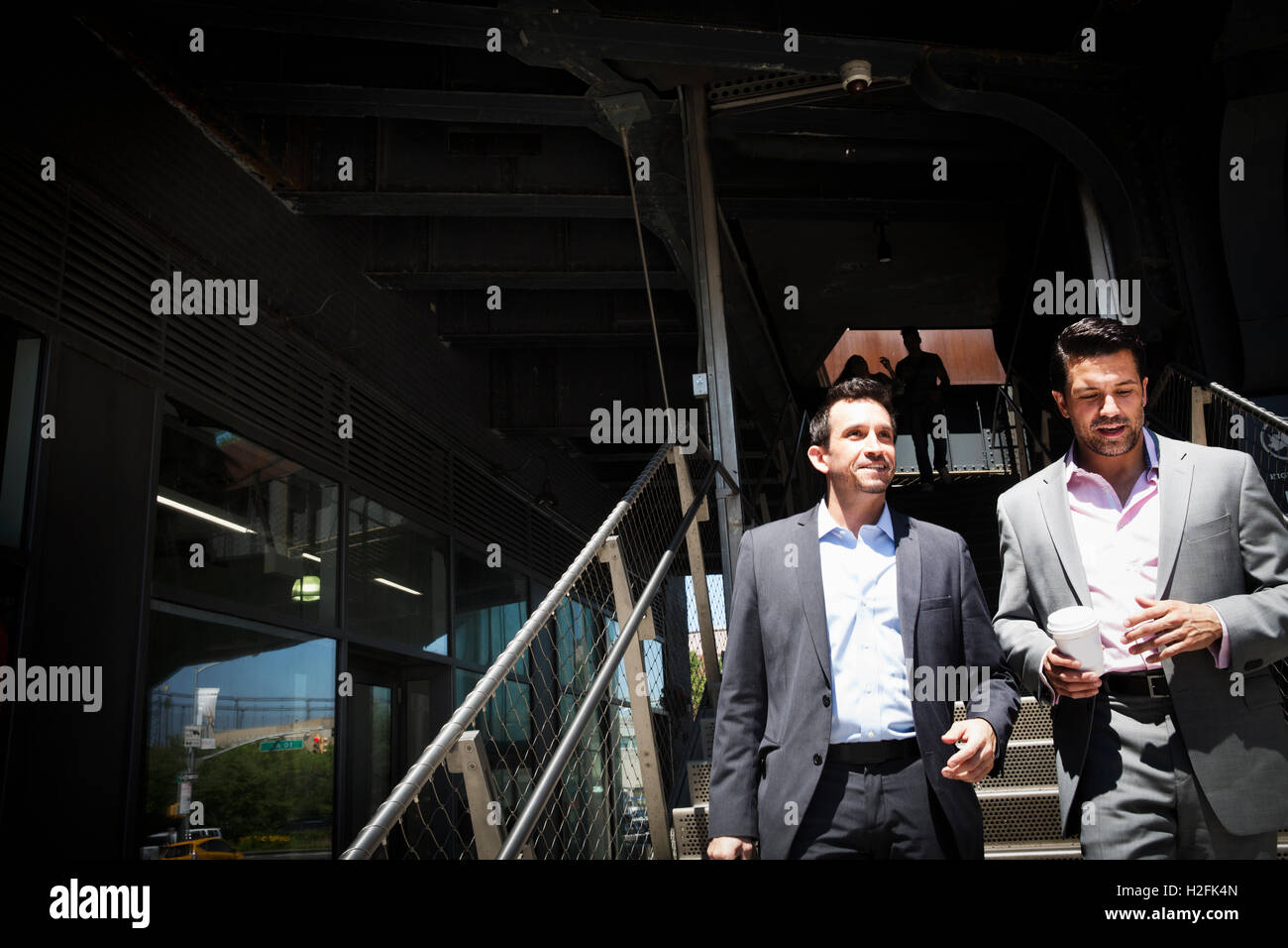 Two businessmen wearing grey suits walking down a staircase at the ...