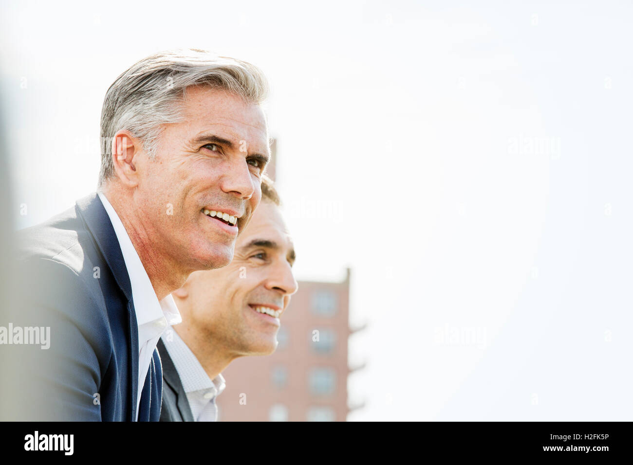 Two people, men talking together outdoors leaning on a railing, taking ...