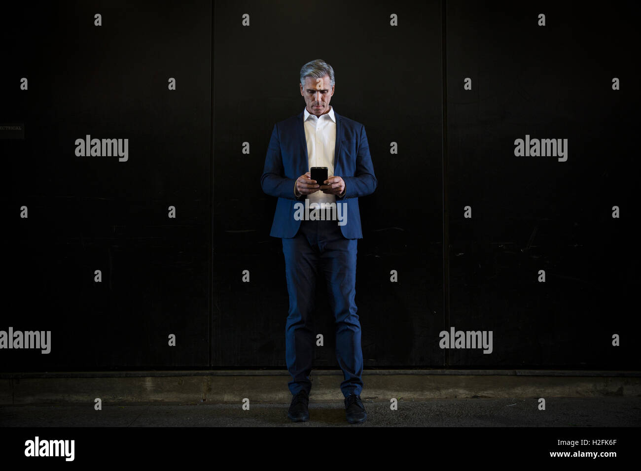 A man in a suit standing in shadow on a city street, looking at his ...