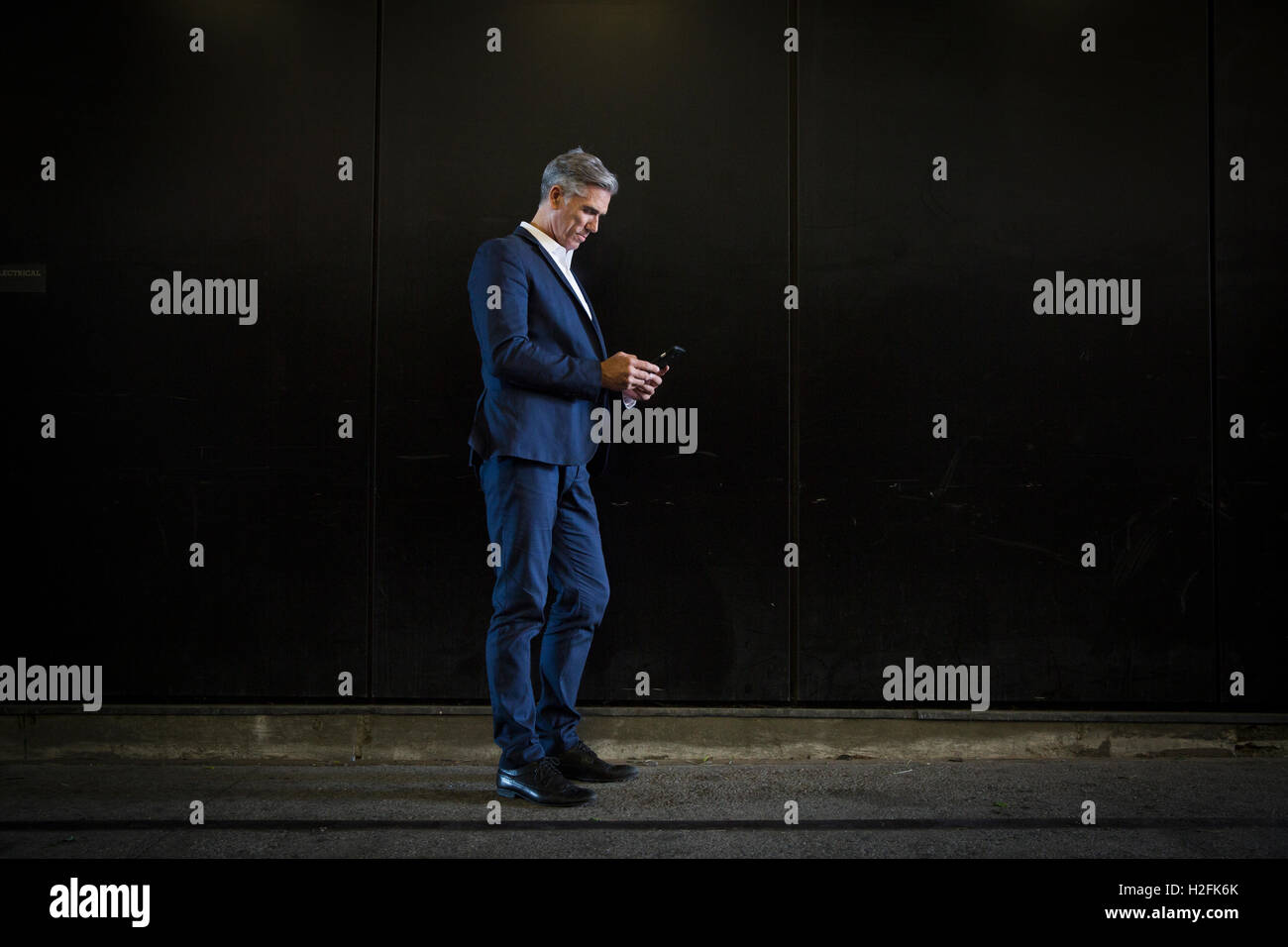 A man in a suit standing in shadow on a city street, looking at his ...