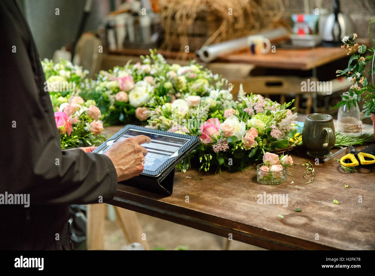 A woman in a florist's workshop using a digital tablet, at a workbench ...