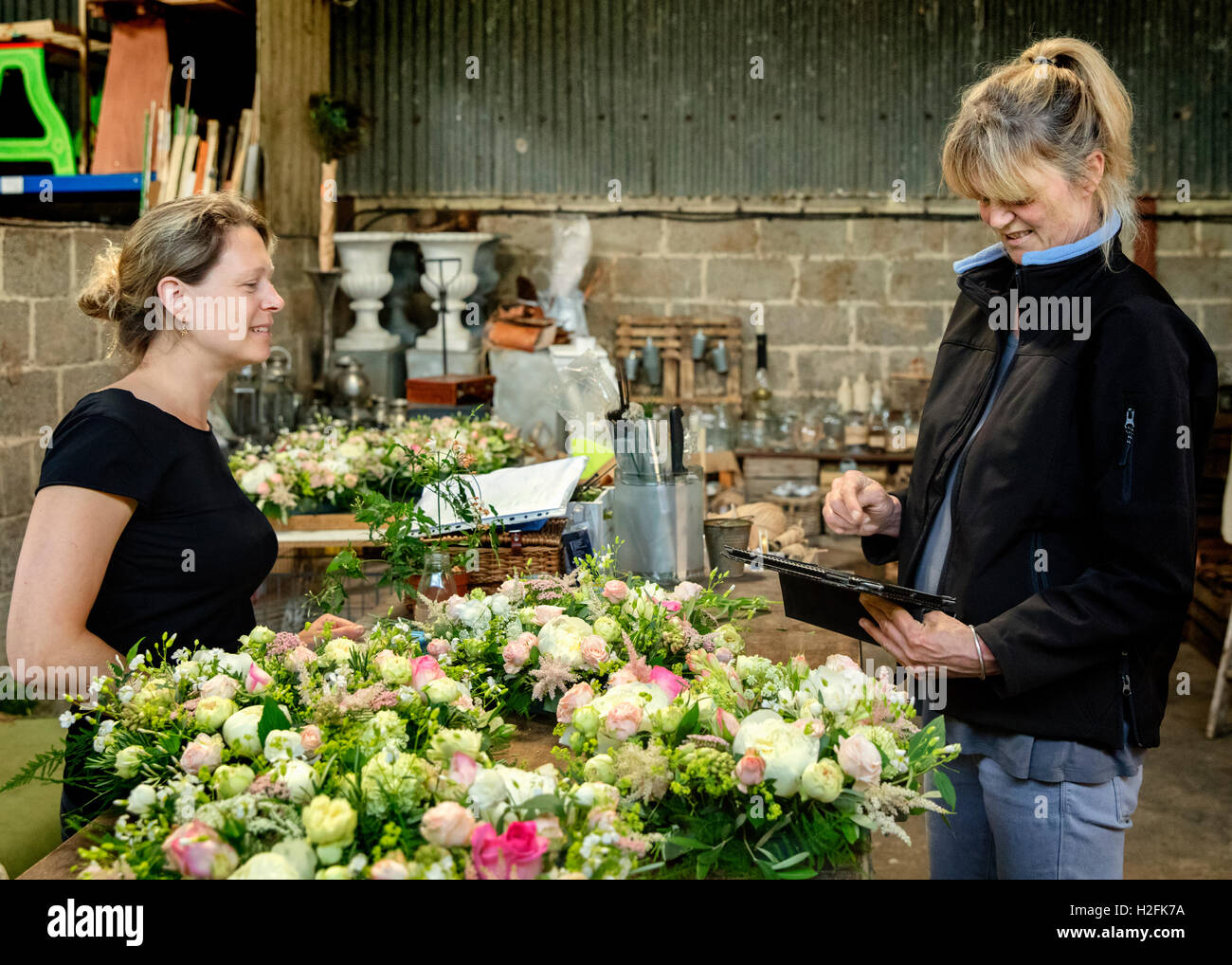 Two women, one using a digital tablet. Florists at a workbench table ...