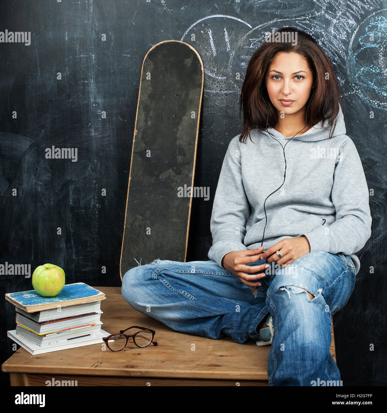 young cute teenage girl in classroom at blackboard seating on table ...