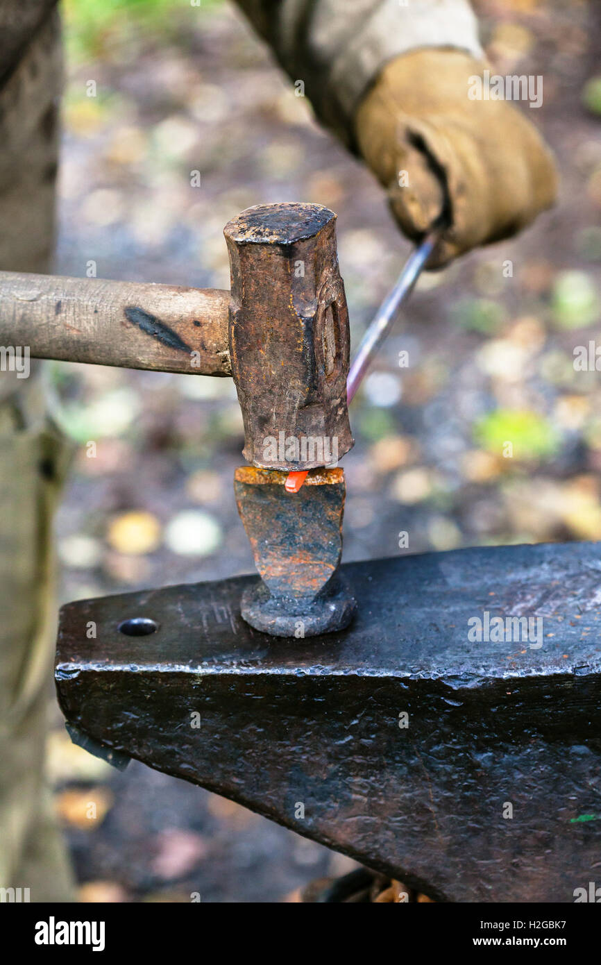 Blacksmith chops hot rod with sledgehammer and chisel on anvil in ...