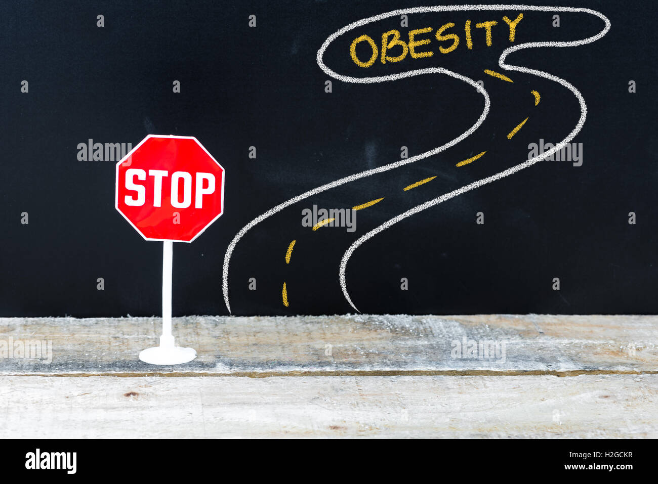 Mini STOP sign on the road to OBESITY, hand drawing over chalkboard ...