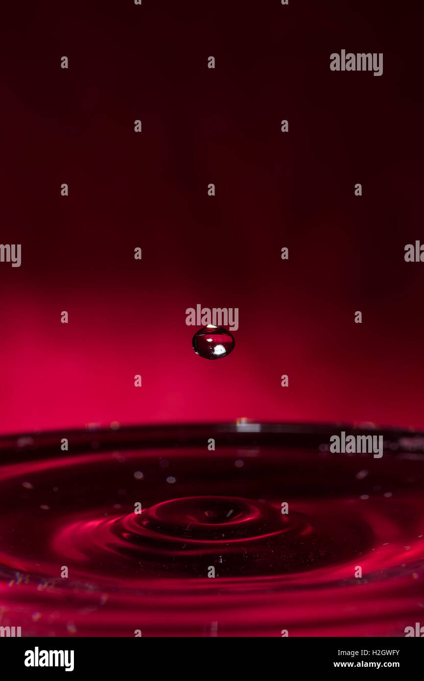 A drop of water falling into a glass filled with water to create a ...