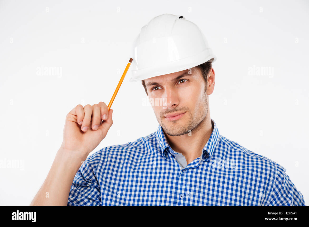 Thoughtful young man builder in building helmet with pencil thinking ...