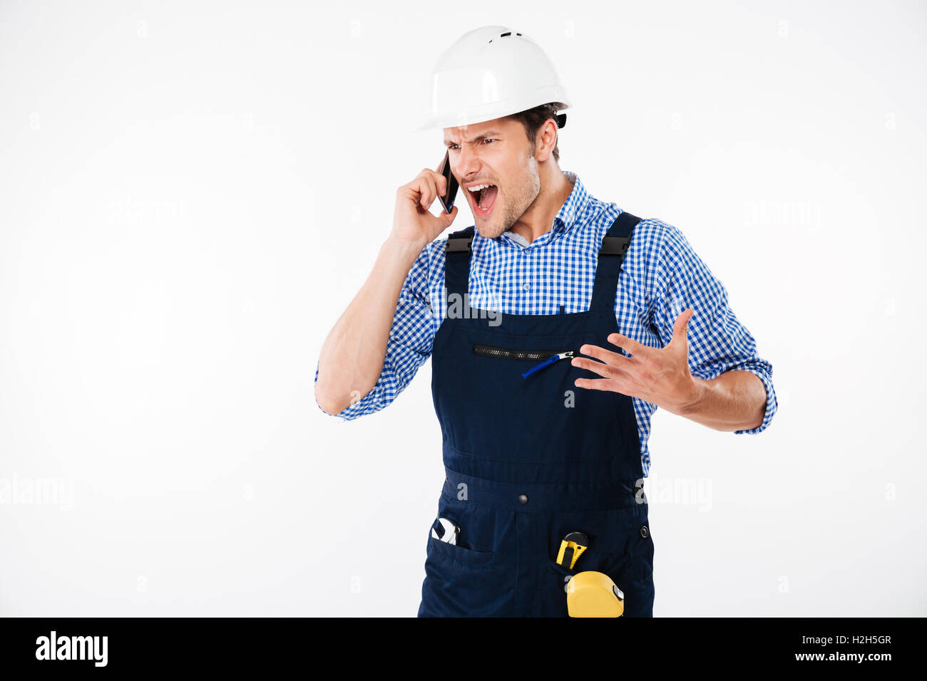 Angry screaming young builder talking on the phone isolated on a white ...