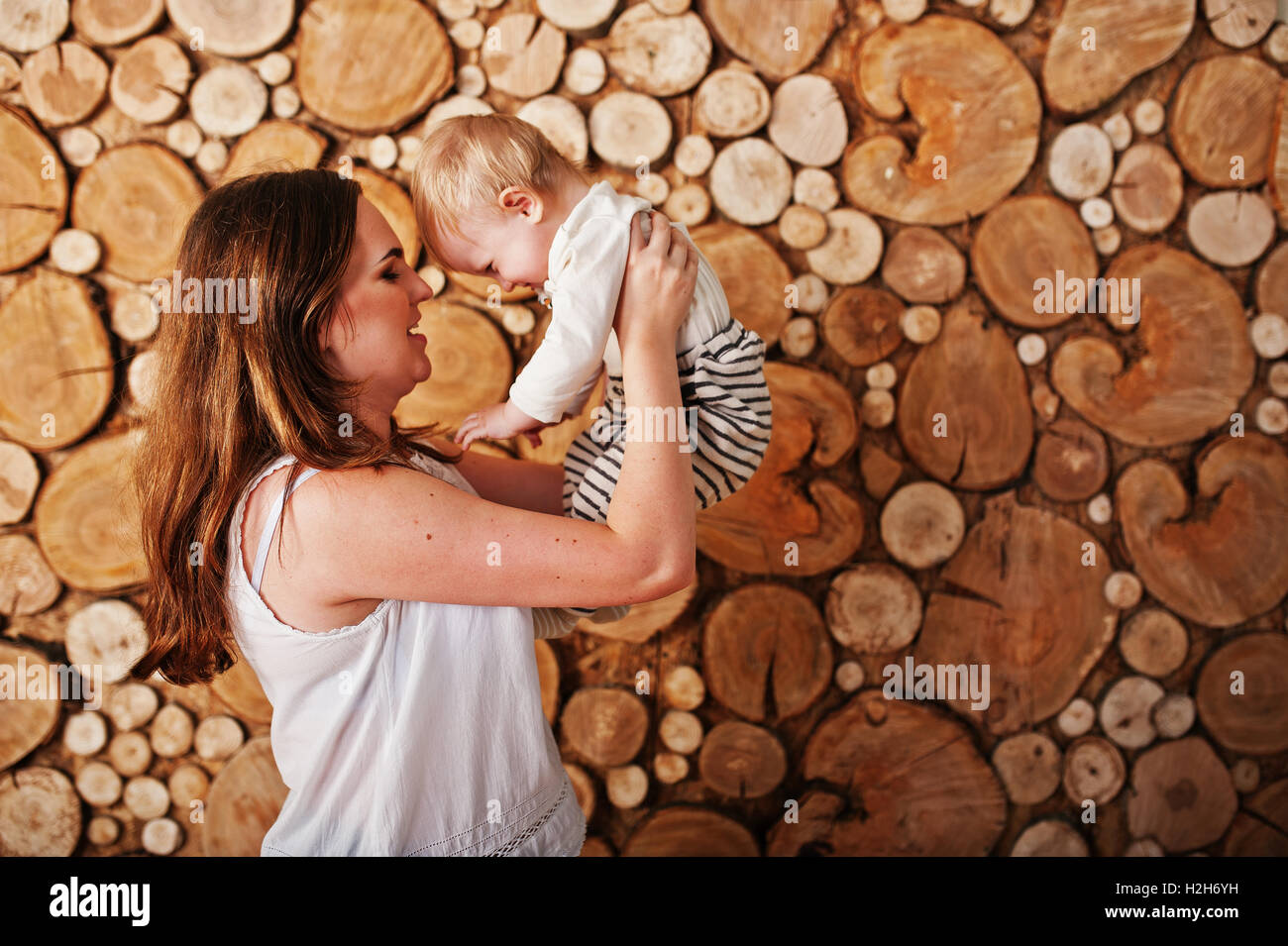 Happy caucasian mother holding on hands her baby boy background stump ...
