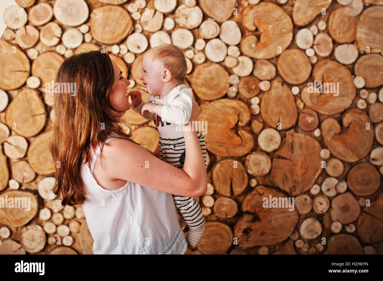 Happy caucasian mother holding on hands her baby boy background stump ...