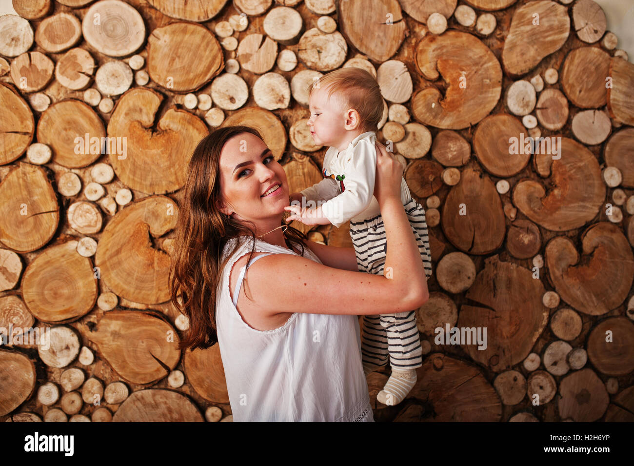Happy caucasian mother holding on hands her baby boy background stump ...