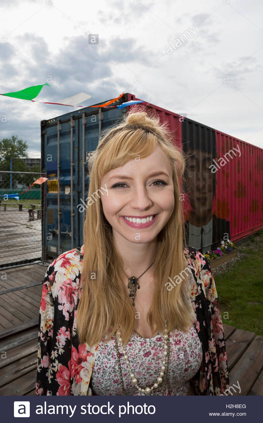 Portrait smiling young blonde woman near painted shipping container ...