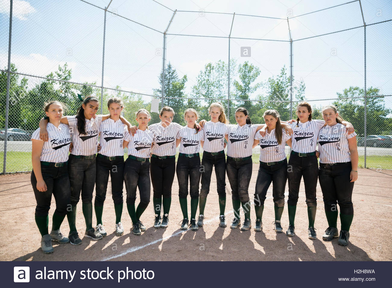 Portrait middle school girl softball team in a row on baseball diamond ...