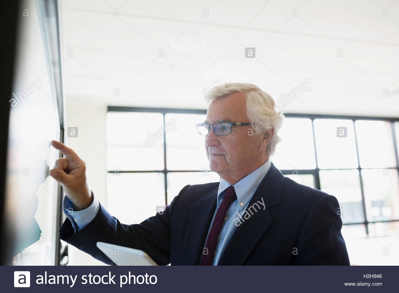 Senior businessman using touch screen television in conference room ...