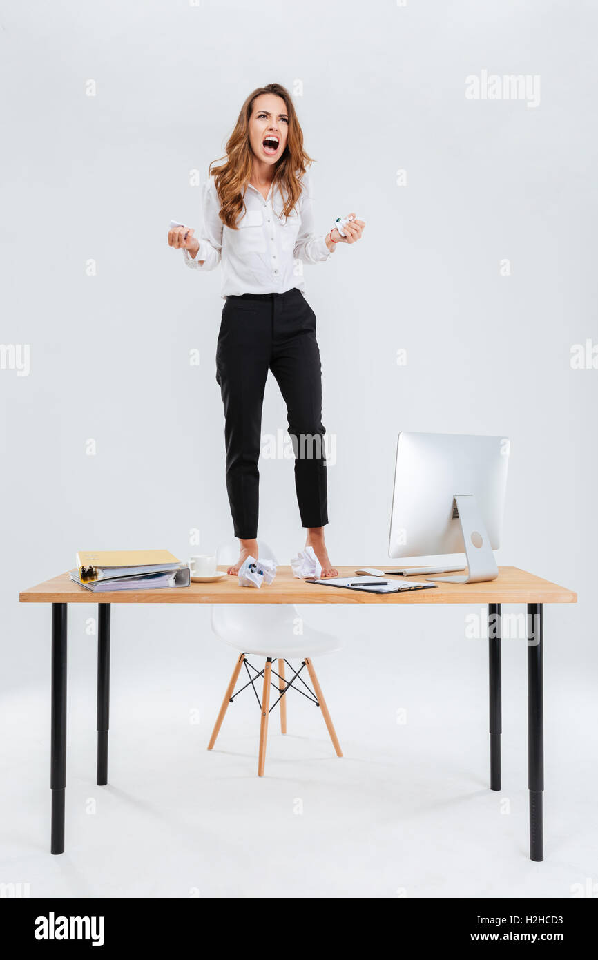 Angry mad young businesswoman standing on table and screaming over ...