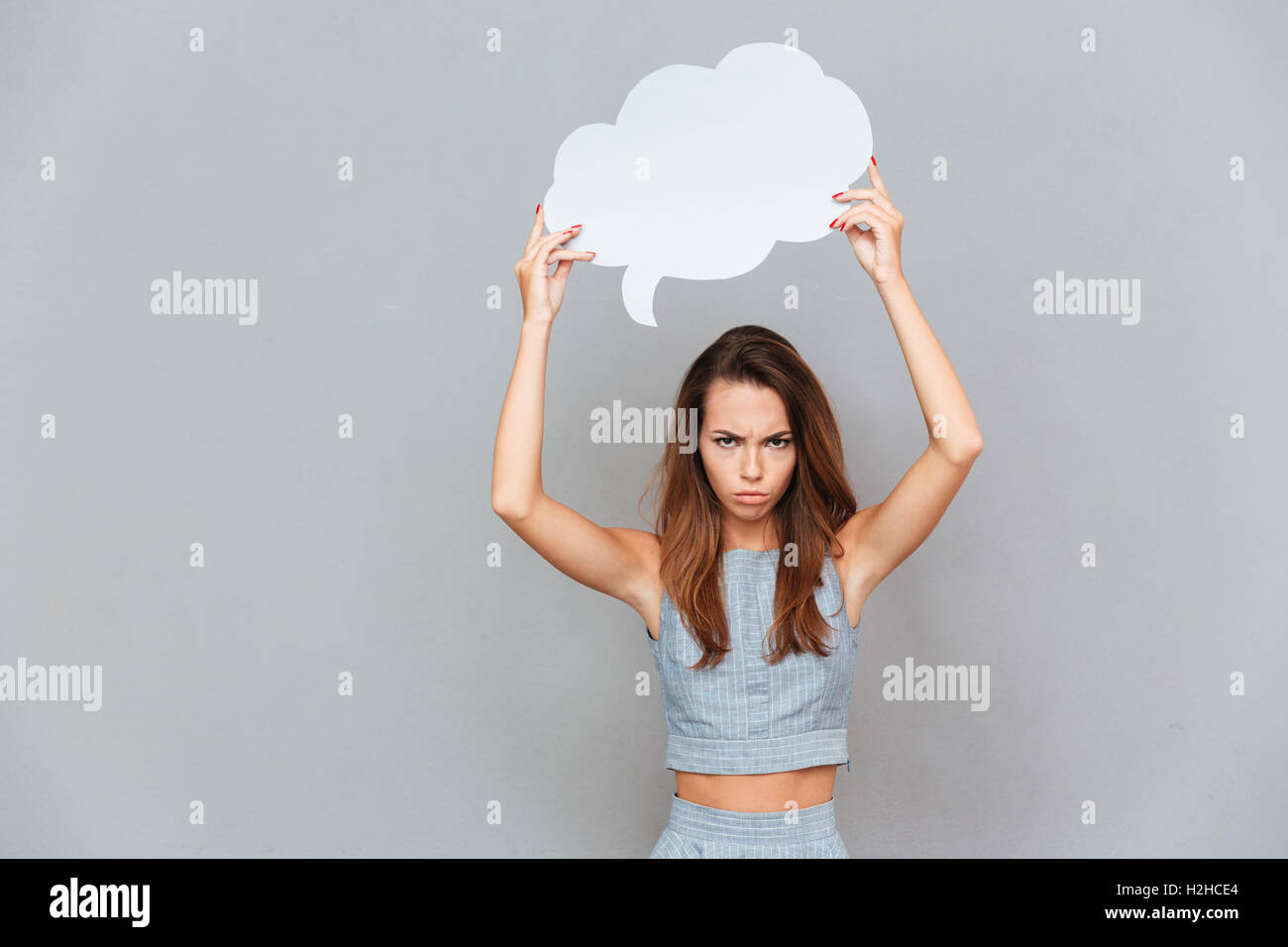 Sad frowning young woman standing and holding empty speech bubble over ...