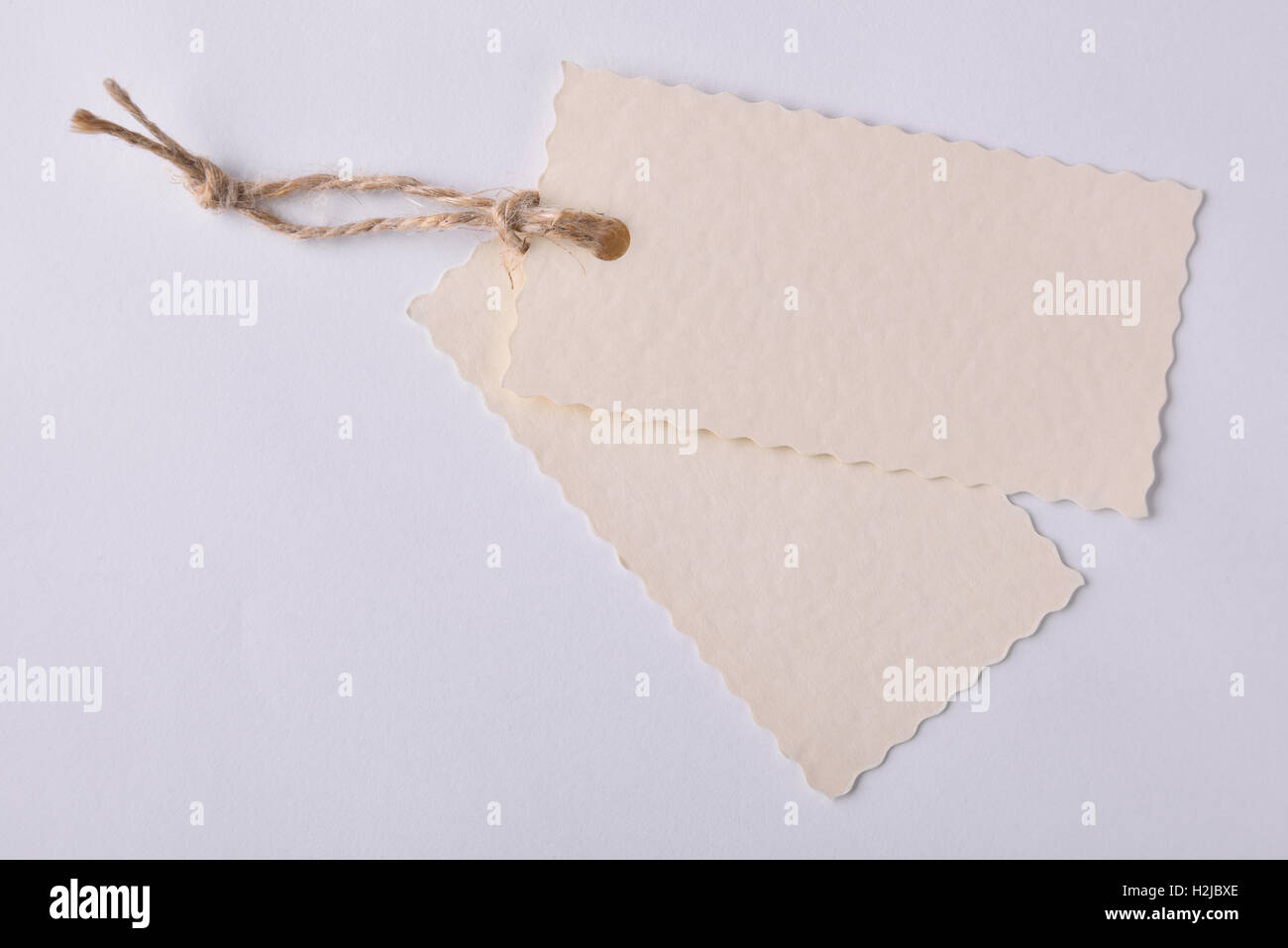 Two beige textured paper tags with string tied on white background. Top ...