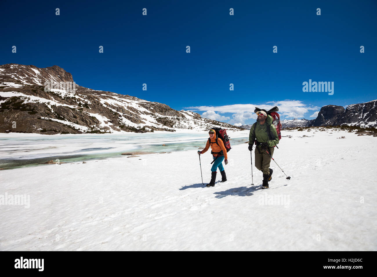 A young woman and man hiking on snow past a frozen lake in the Wind ...