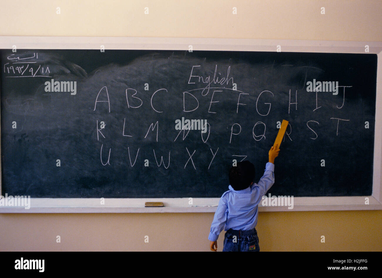 A young boy working at the blackboard points to letters during a class ...