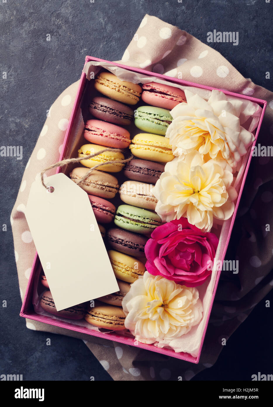Colorful macaroons and flowers on stone table. Sweet macarons in gift ...