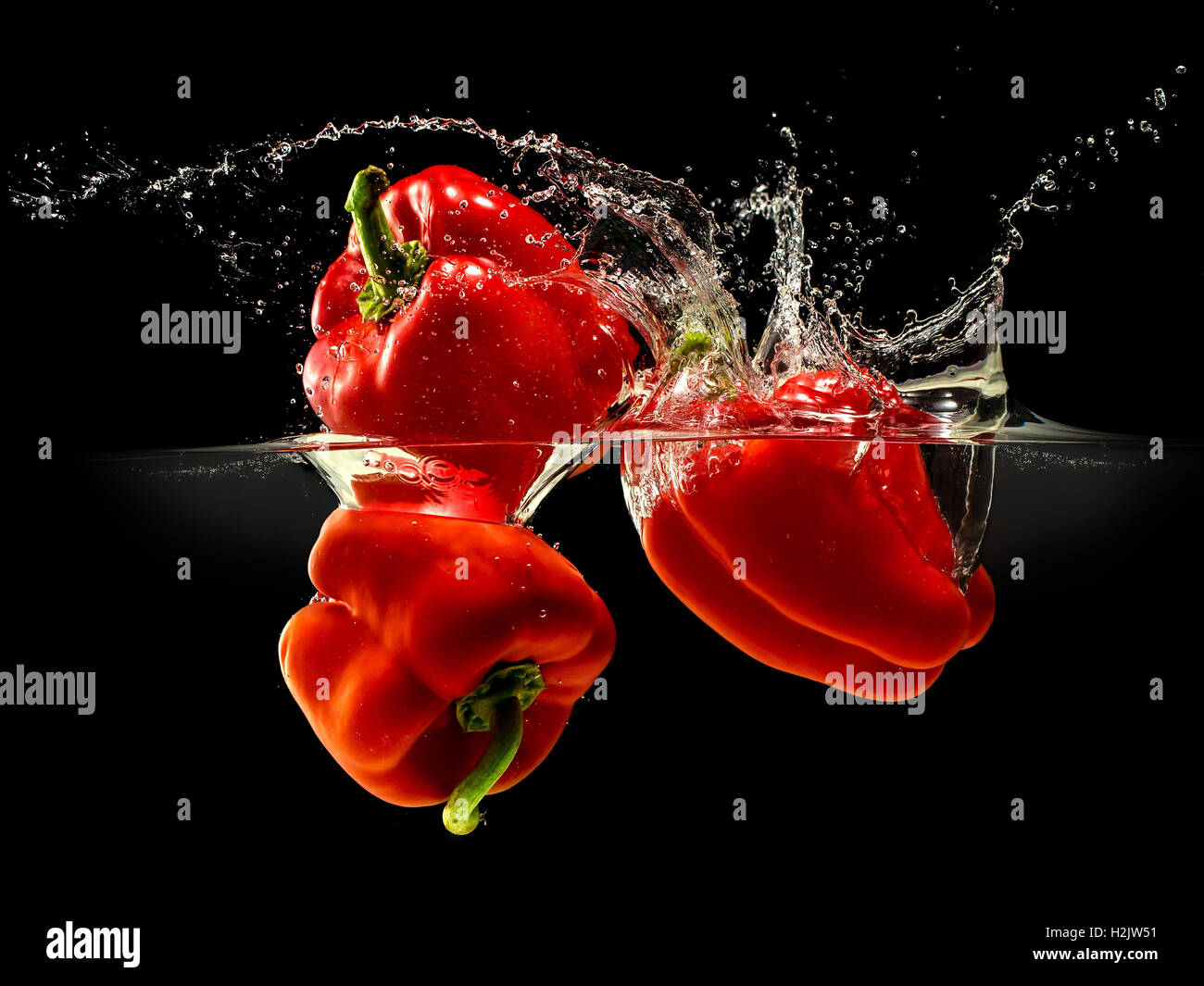 Group of bell pepper falling in water with splash on black background ...