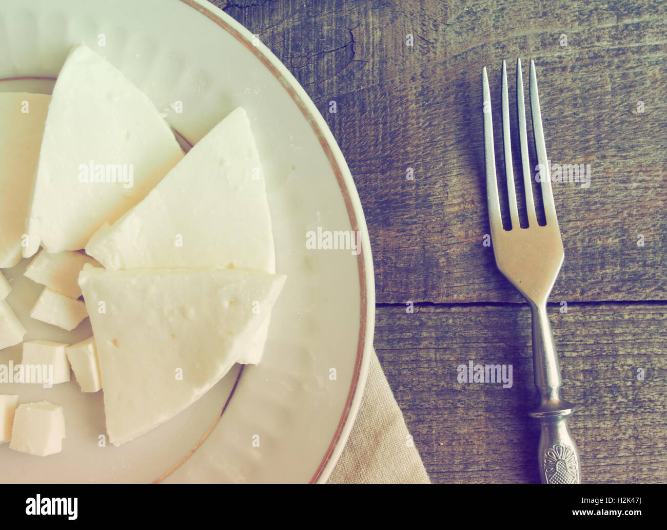 Pieces of soft white cheese on plate and vintage fork over wooden ...
