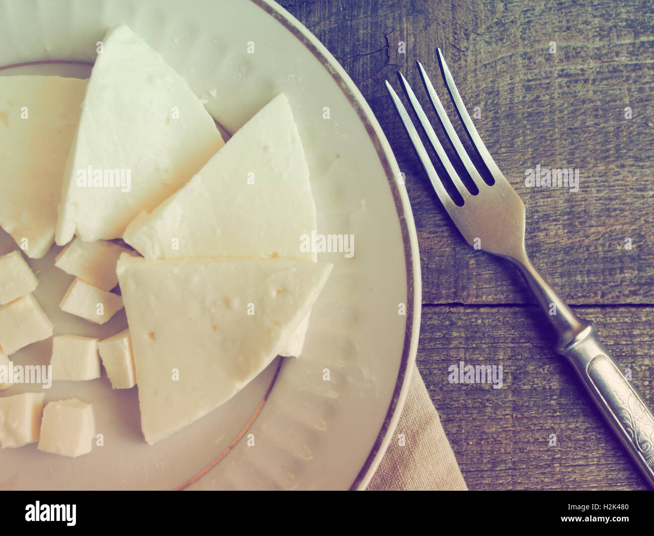 Pieces of soft white cheese on plate and vintage fork over wooden ...