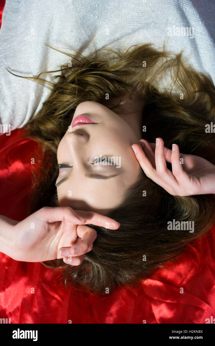 Beautiful young woman laying down hands touching face looking away ...