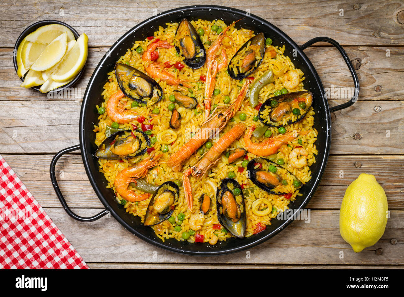 Spanish paella on a wooden table with fresh lemon and a white and red ...