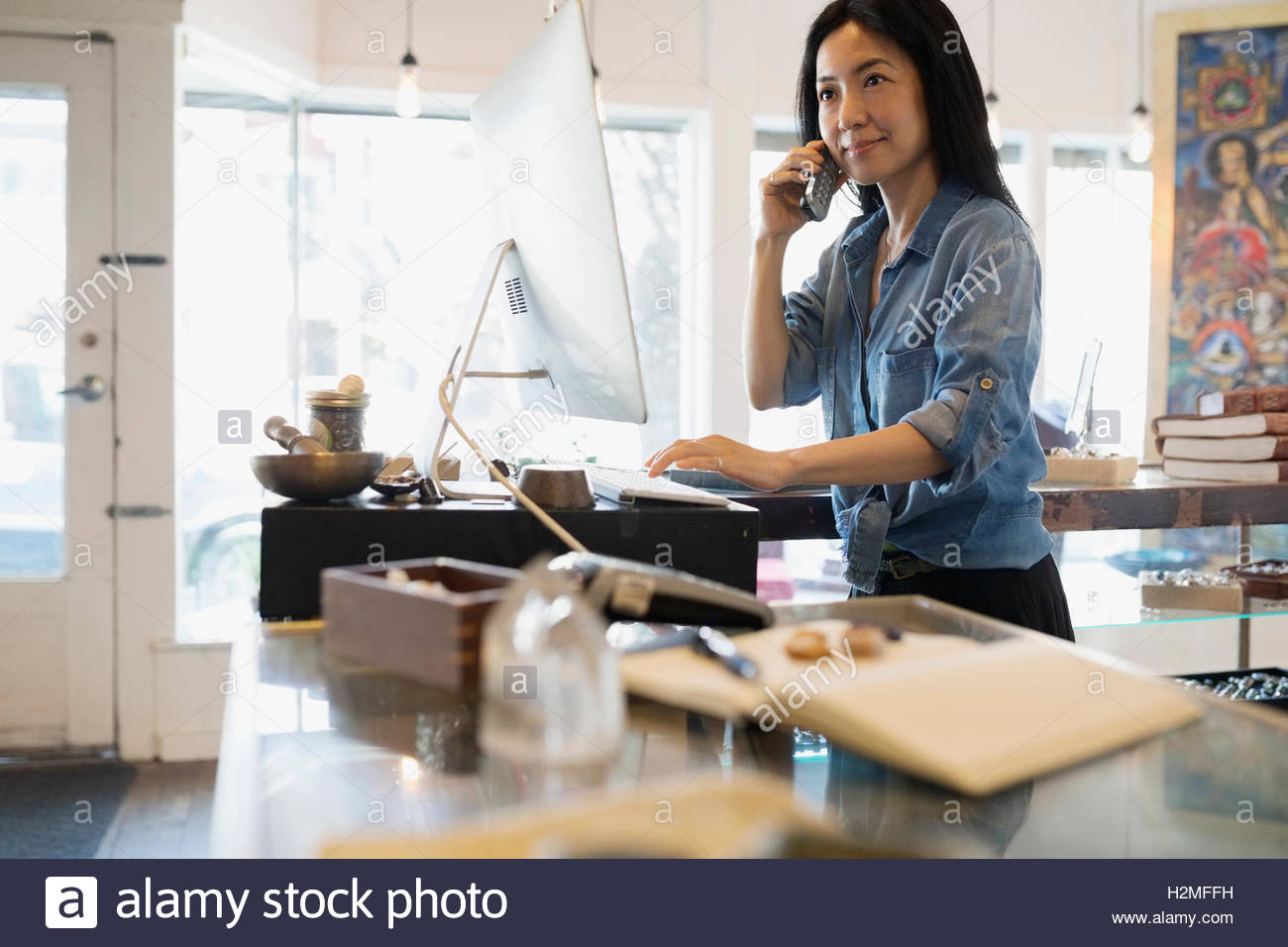 Female shop owner talking on telephone at computer behind counter Stock ...