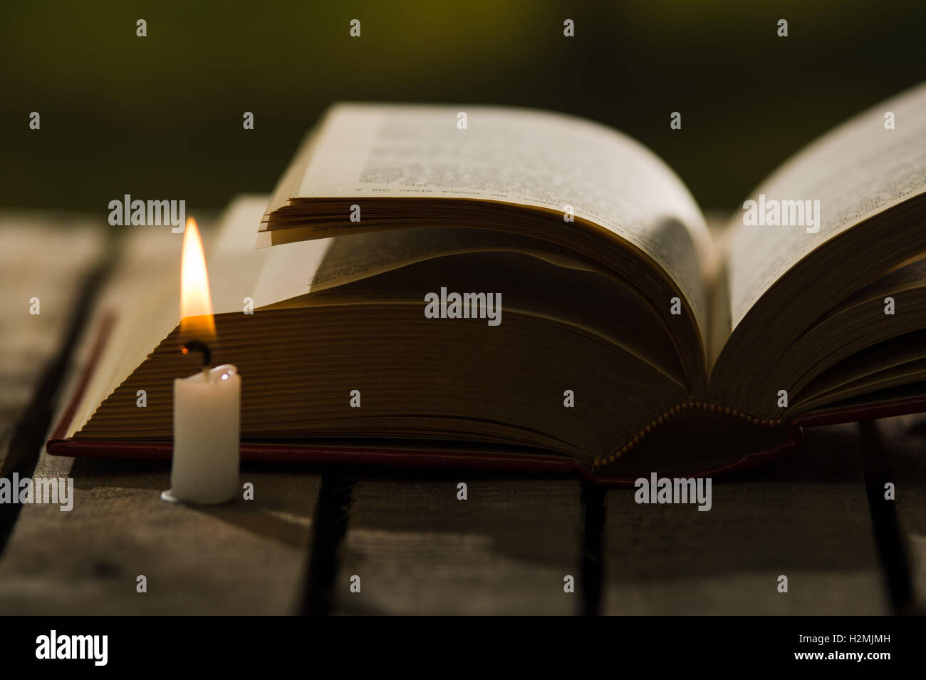 Thick book lying open on wooden surface, wax candle sitting next to it ...