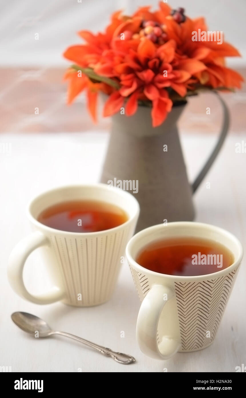 Two mugs of hot tea with vibrant Fall flower arrangement in rustic jug ...