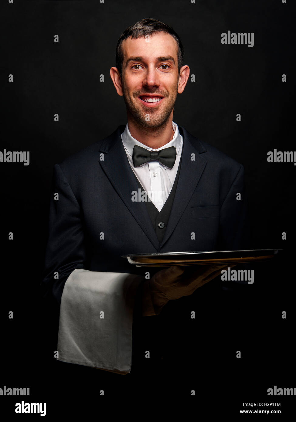 Waiter in black suit holding tray over black background Stock Photo - Alamy