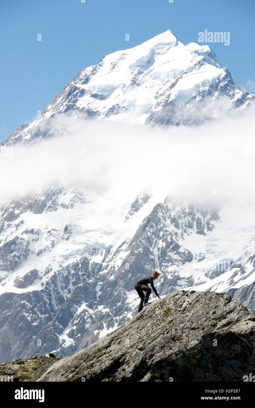 A man scrambling up a rock with Mount Cook looming Stock Photo - Alamy