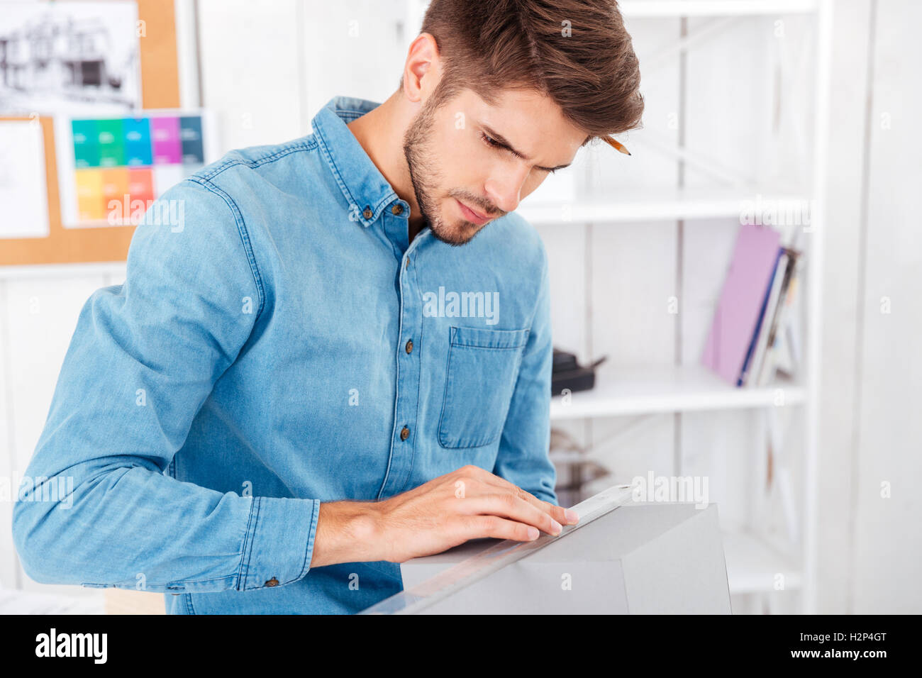 Concentrated young man measuring box with ruller while sitting at the ...