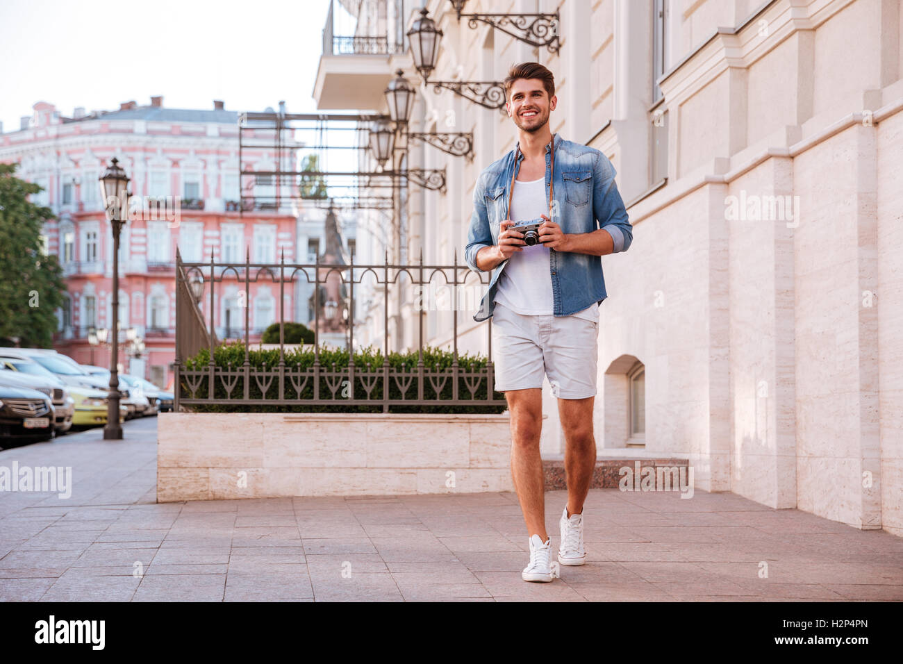 Full length of happy young man with photo camera walking on the street ...