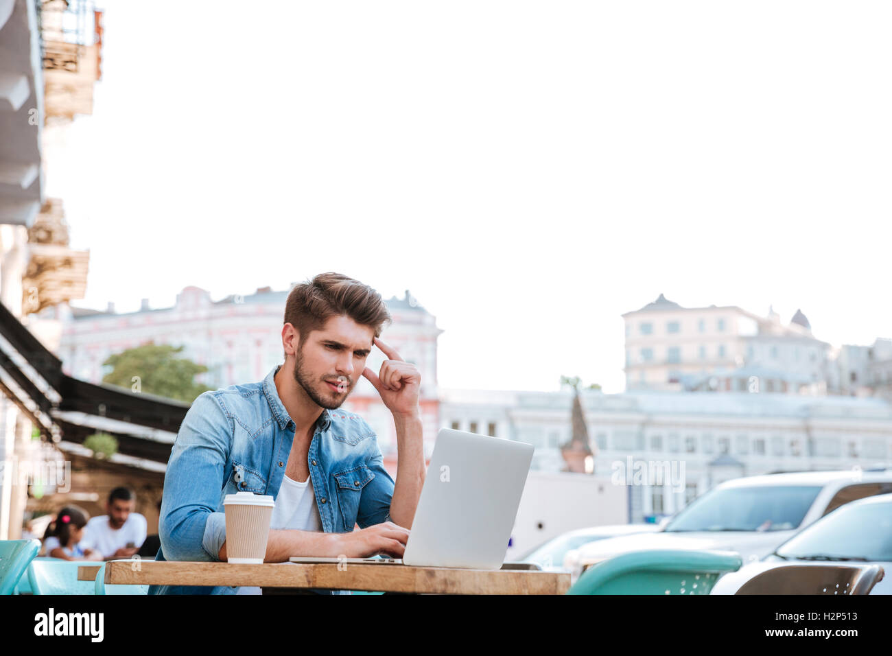 Thoughtful young casual man looking at laptop while sitting in cafe ...