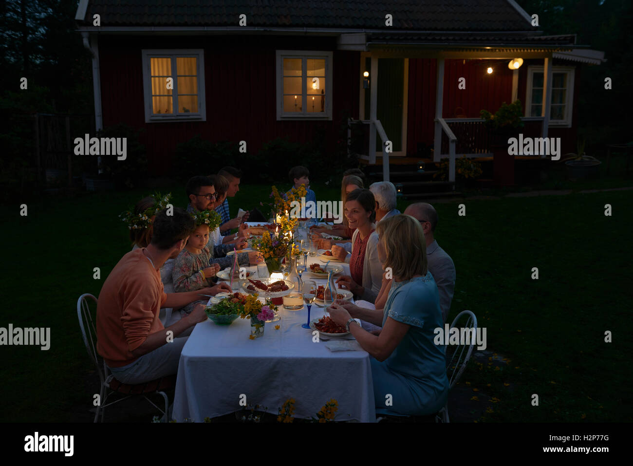 Family enjoying candlelight dinner at patio table outside house at ...