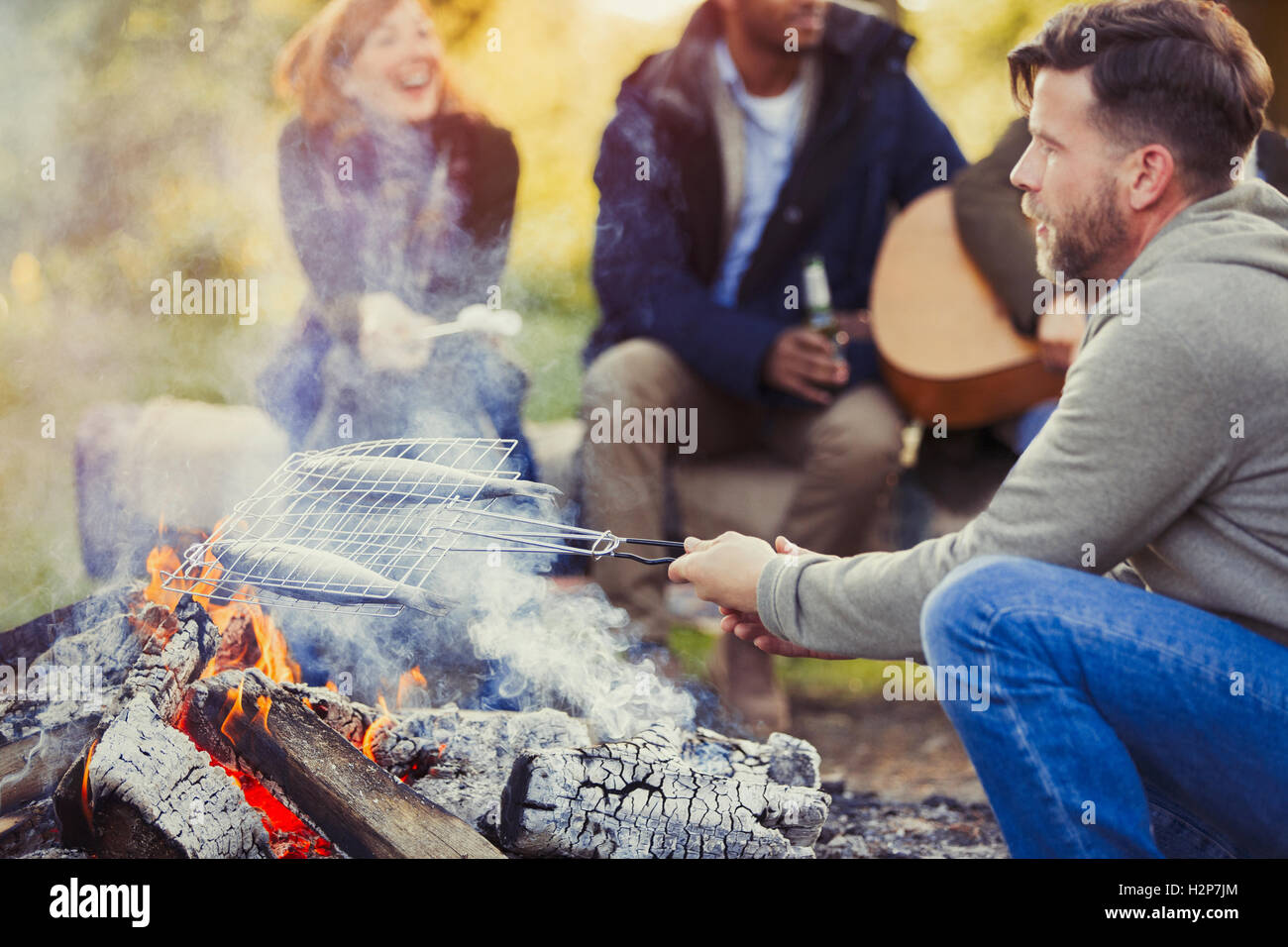 Man frying fish in grill basket over campfire near friends Stock Photo ...