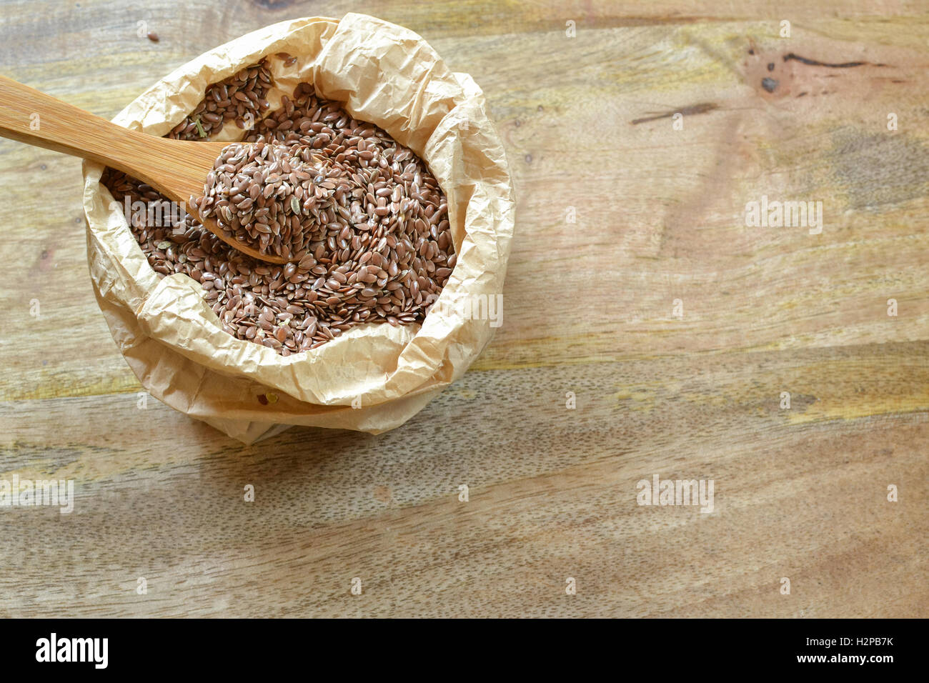 Wooden spoon picking up bunch of flax seeds from paper bag, on wooden ...